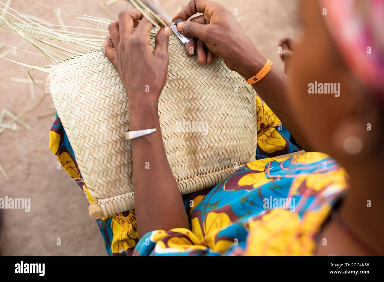 A Fulani woman weaves matts and fans from dried palm fronds by hand for ...