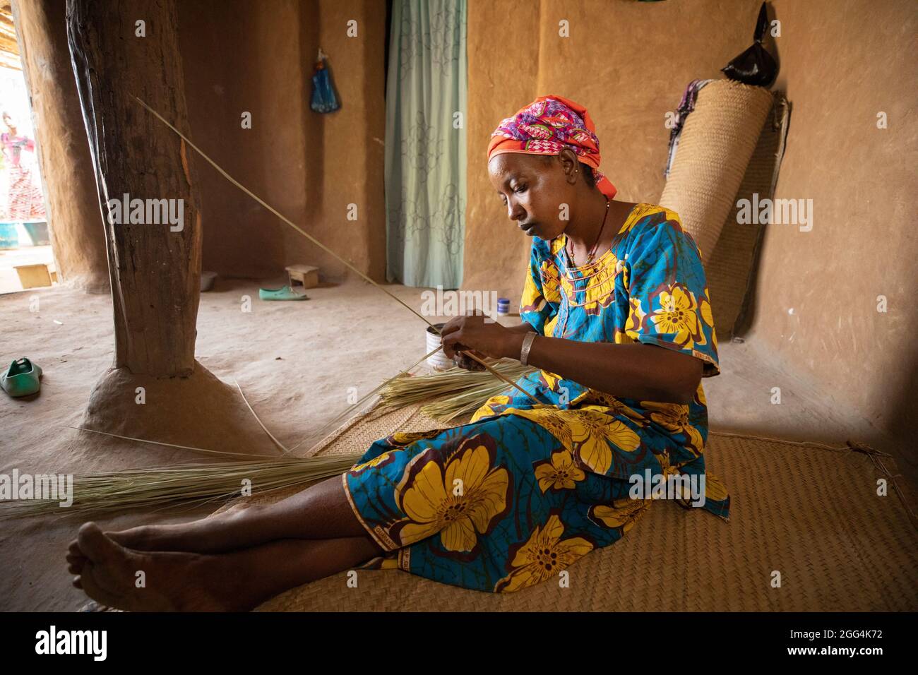A Fulani woman weaves matts and fans from dried palm fronds by hand for ...