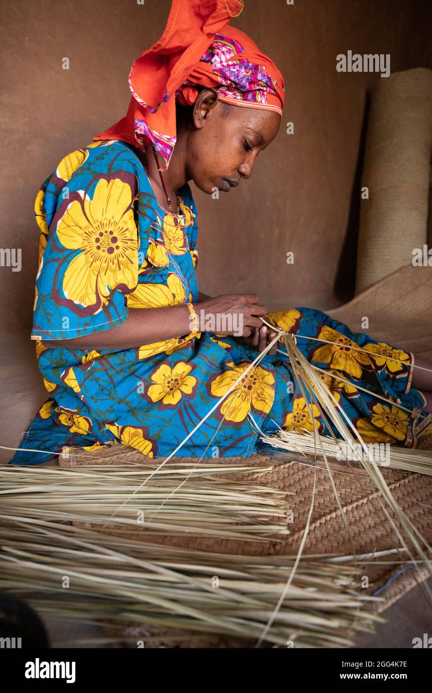 A Fulani woman weaves matts and fans from dried palm fronds by hand for ...