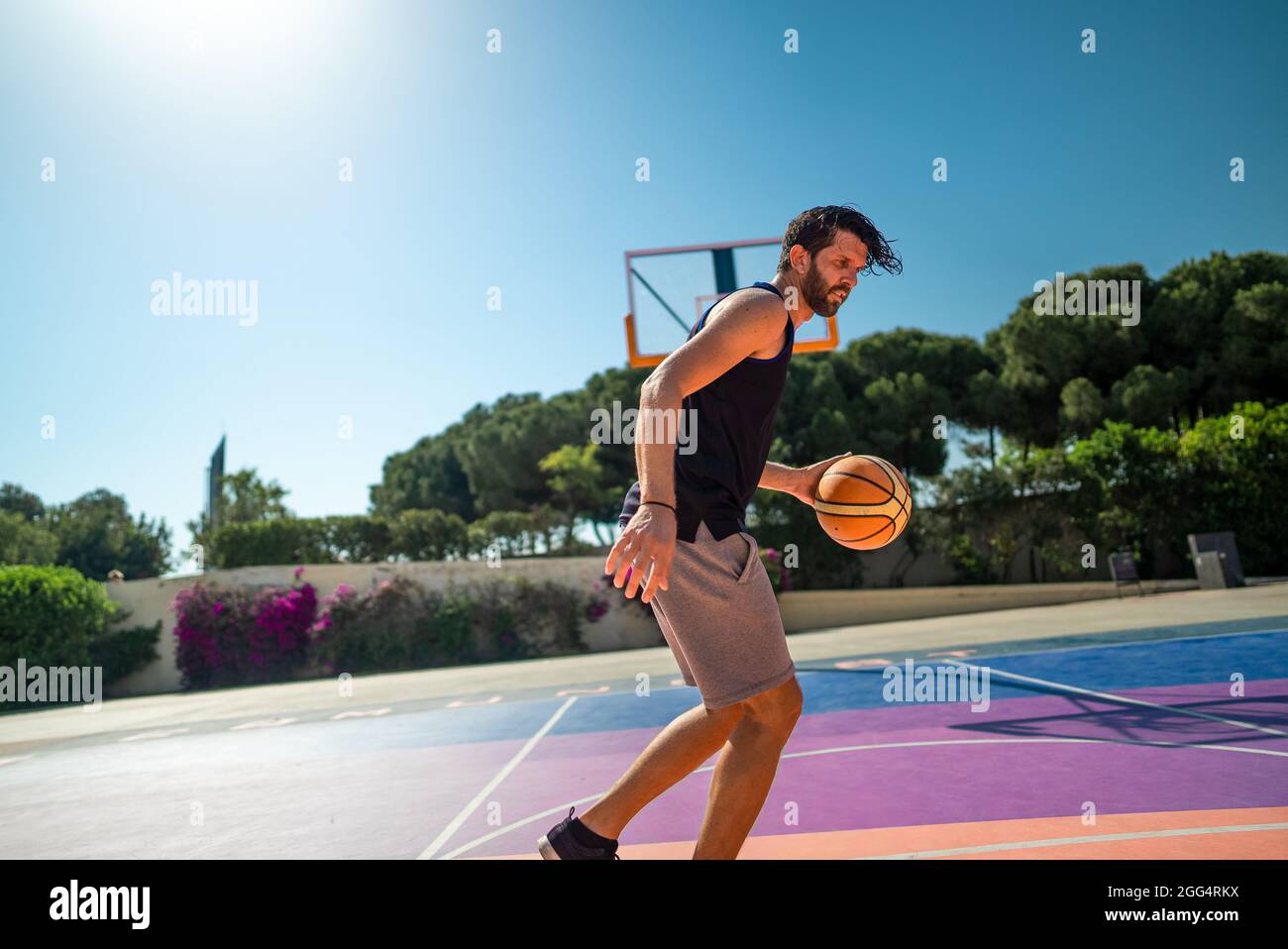 A male basketball player trains himself on a basketball court with a ...