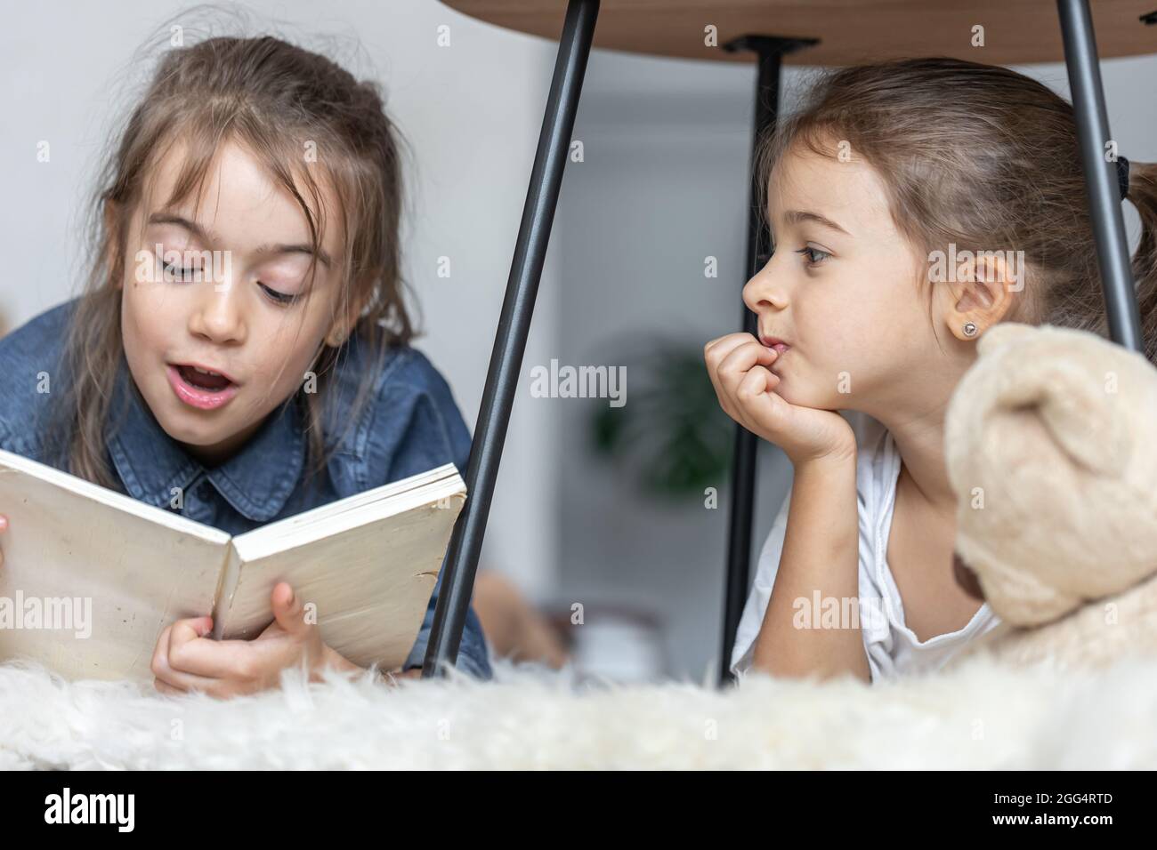 Two little sisters have fun reading a book together while lying on the ...