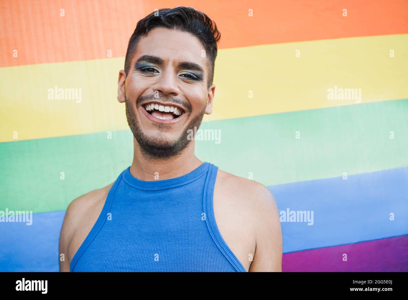 Young transgender man with makeup smiling on camera with lgbt rainbow ...