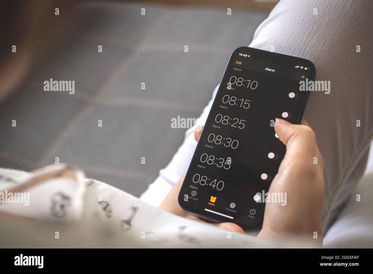 Woman set alarm for wake up on her mobile phone sitting on sofa at home ...