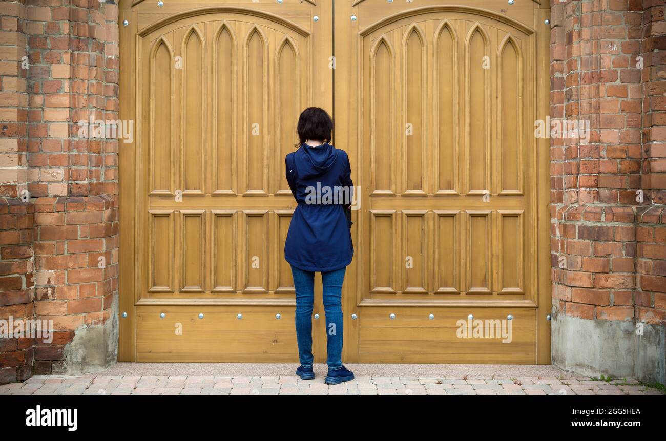 A woman is facing the huge gate of a Catholic church trying to open the ...