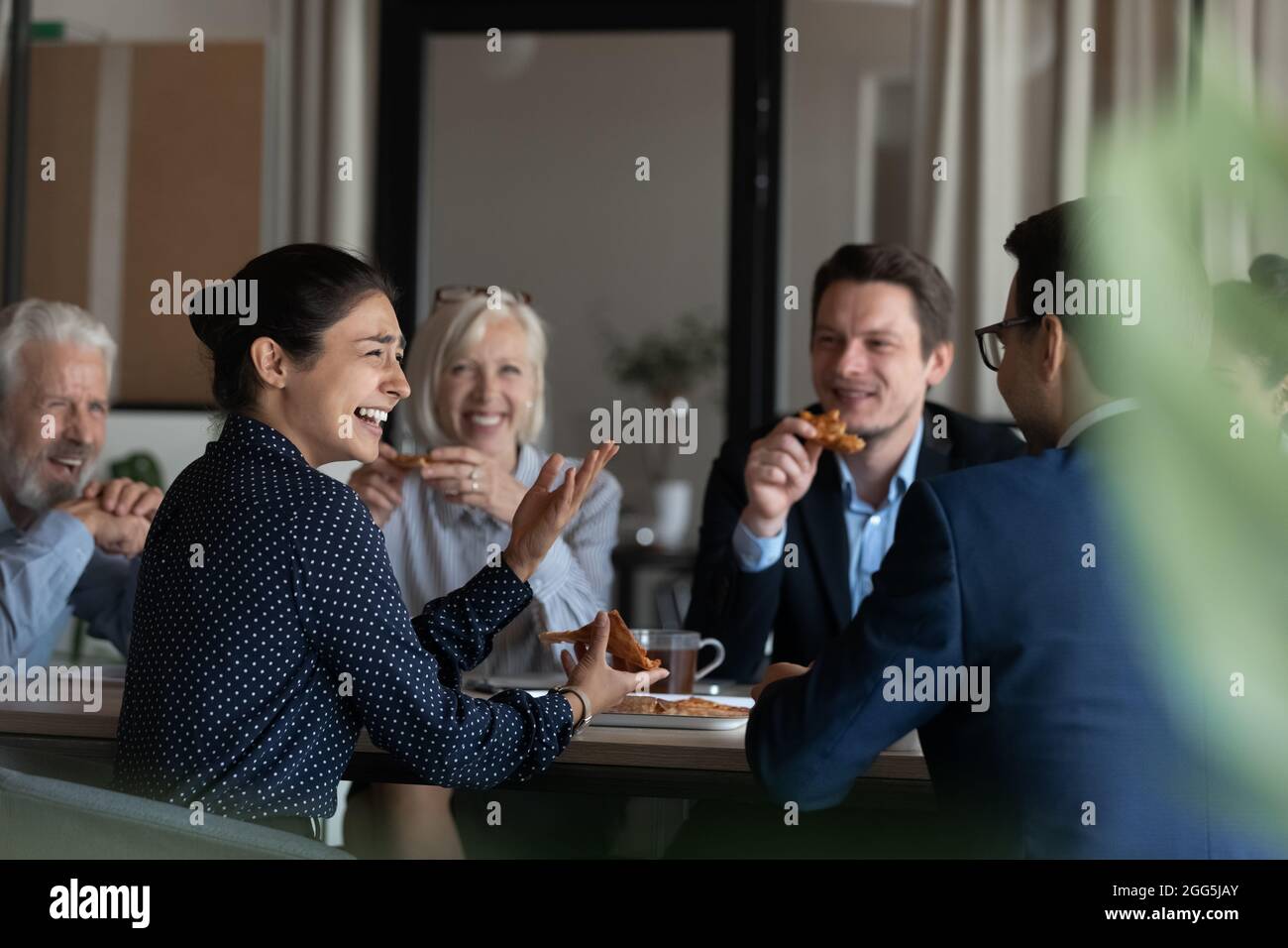 Excited diverse employees eating pizza during break in office together ...