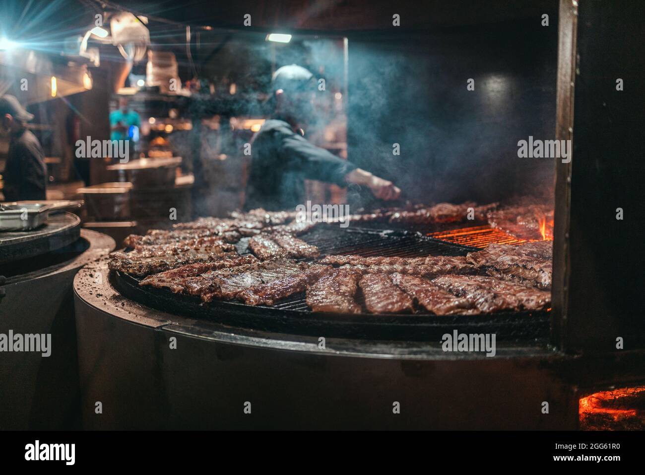 Professional chef grills pork or beef ribs on an open round grill oven ...