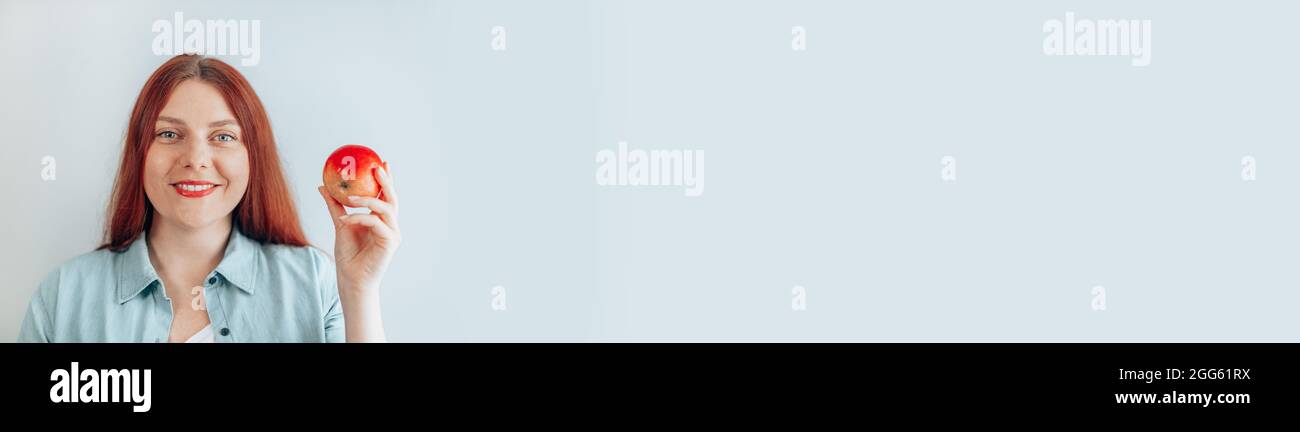 Portrait of a cheerful young woman eating red apple on gray wall ...