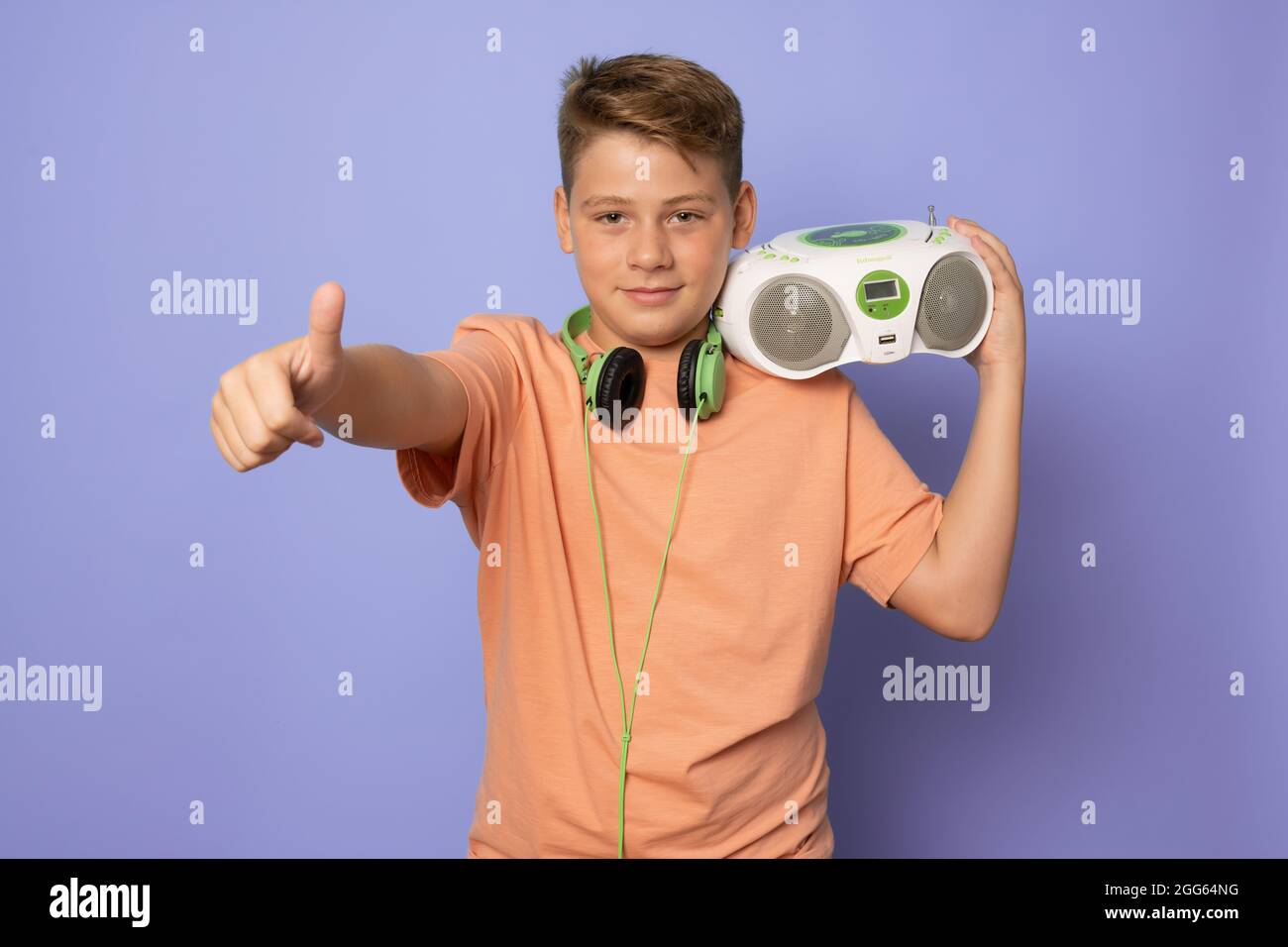 Young boy holding a radio cassette with thumb up isolated over purple ...