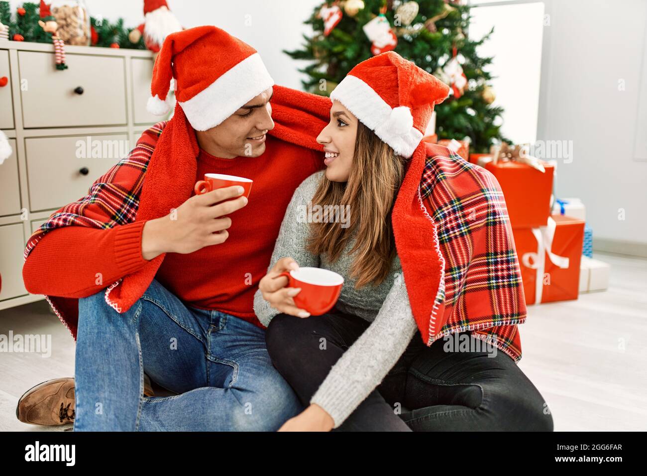 Young couple wearing christmas hat covering with blanket. Sitting on ...