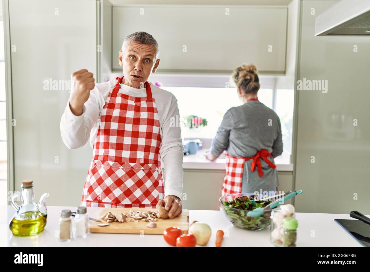 Middle age caucasian couple cooking healthy salad annoyed and ...