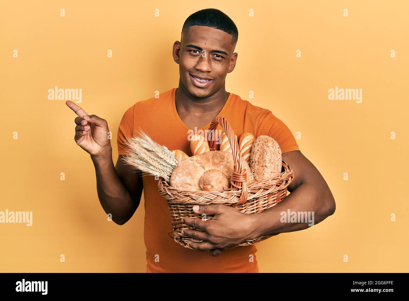 Young black man holding wicker basket with bread smiling happy pointing ...