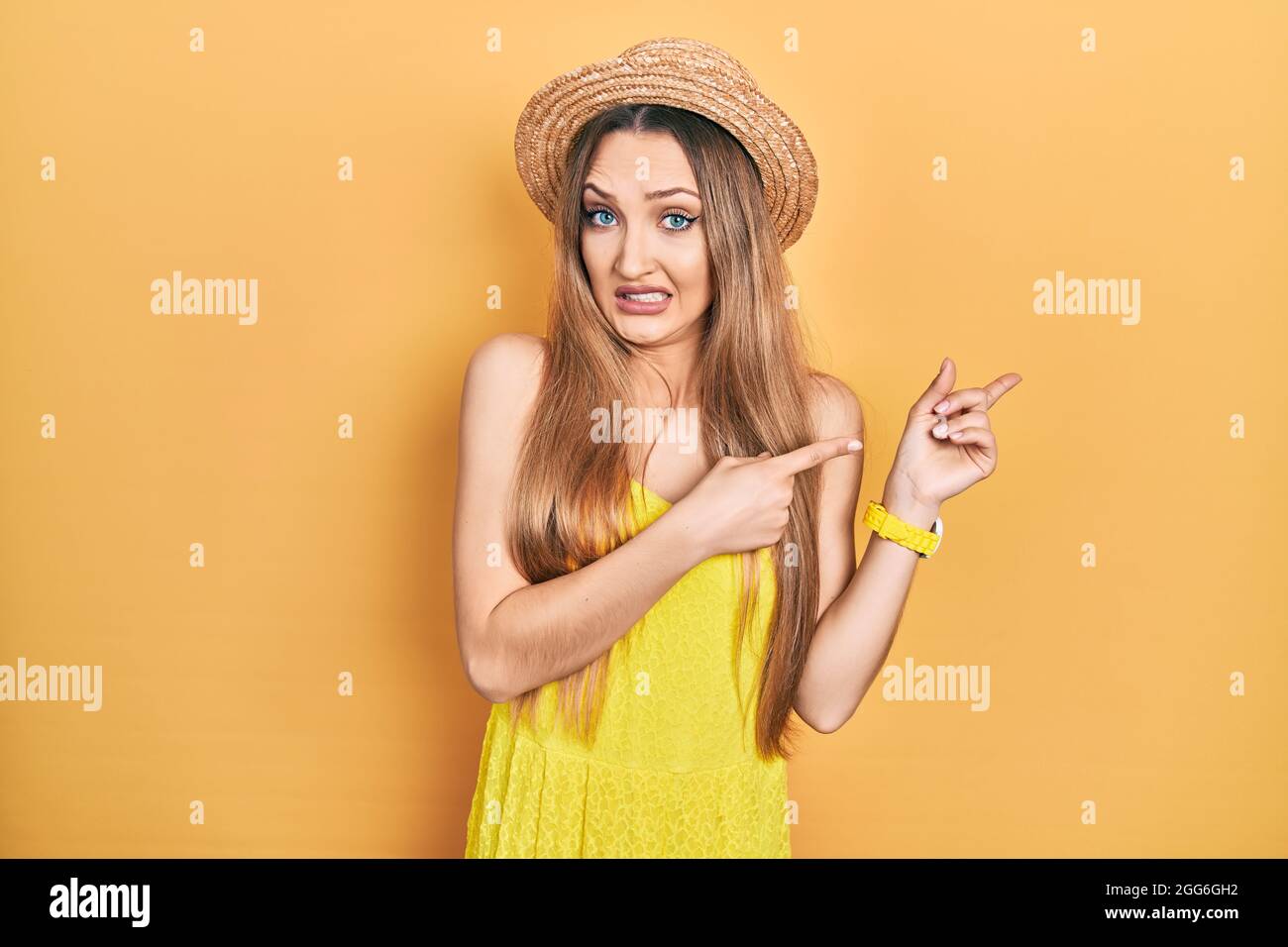 Young blonde girl wearing summer hat pointing aside worried and nervous ...