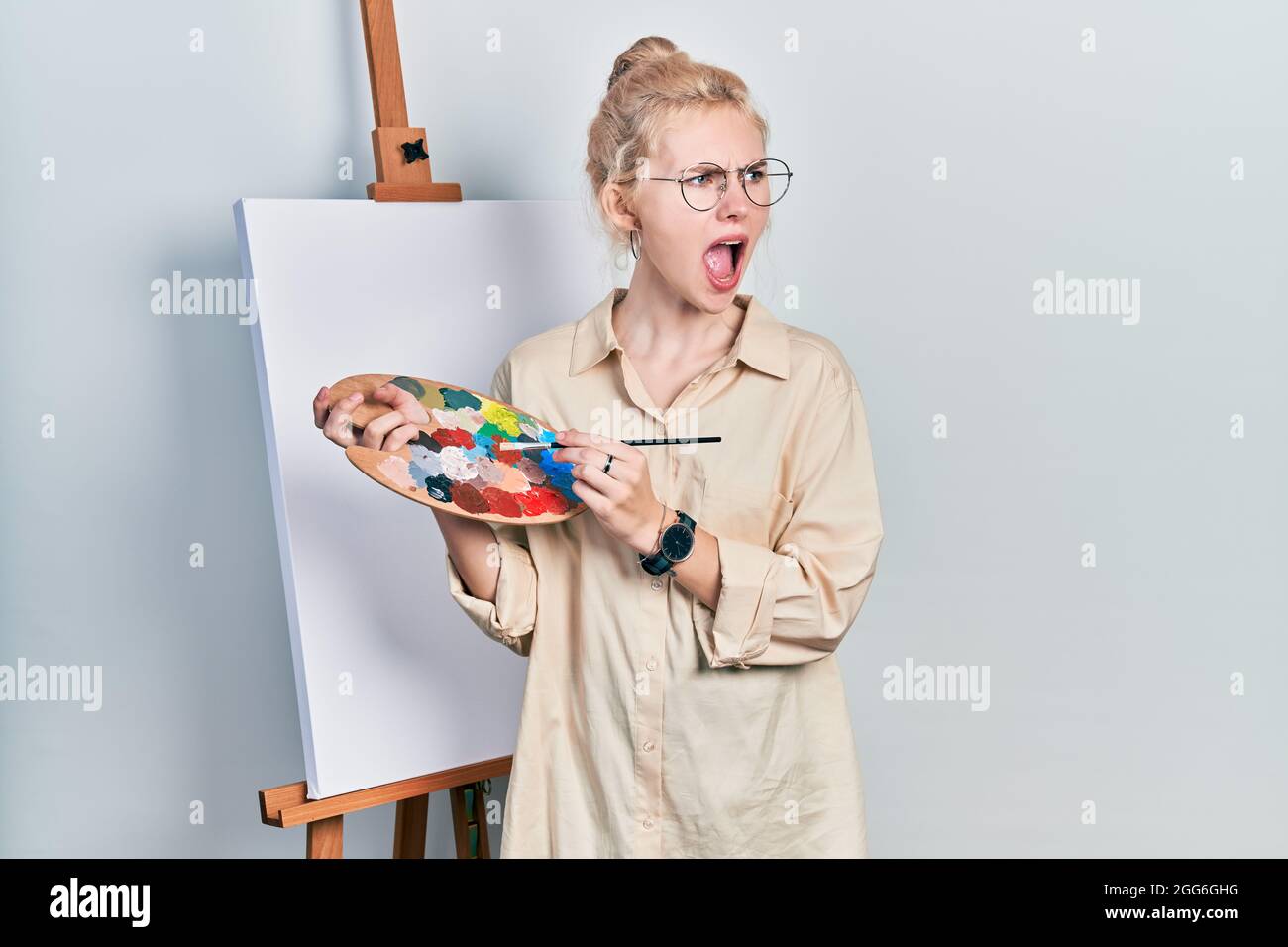 Beautiful caucasian woman with blond hair standing drawing with palette ...