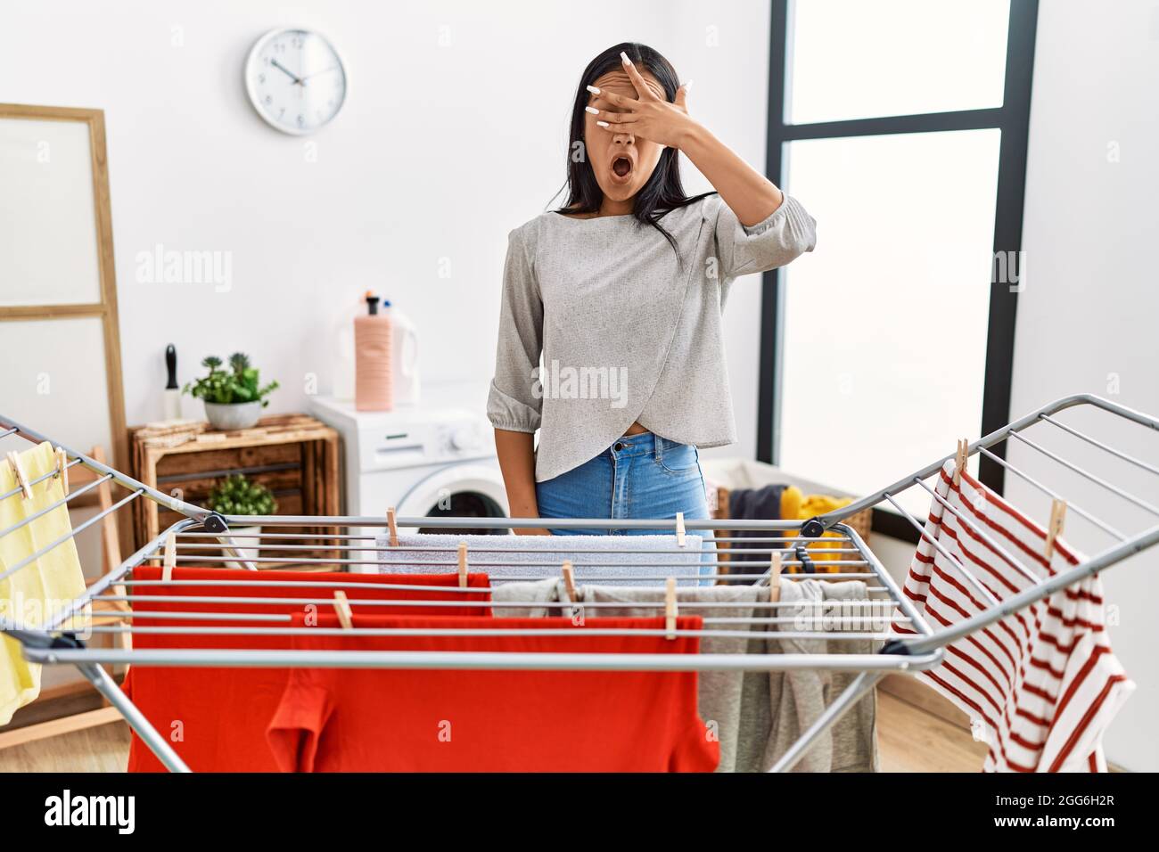 Young hispanic woman putting fresh laundry on clothesline peeking in ...