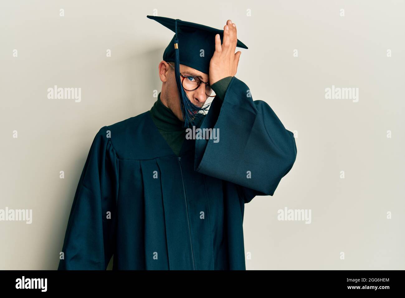 Young caucasian man wearing graduation cap and ceremony robe surprised ...