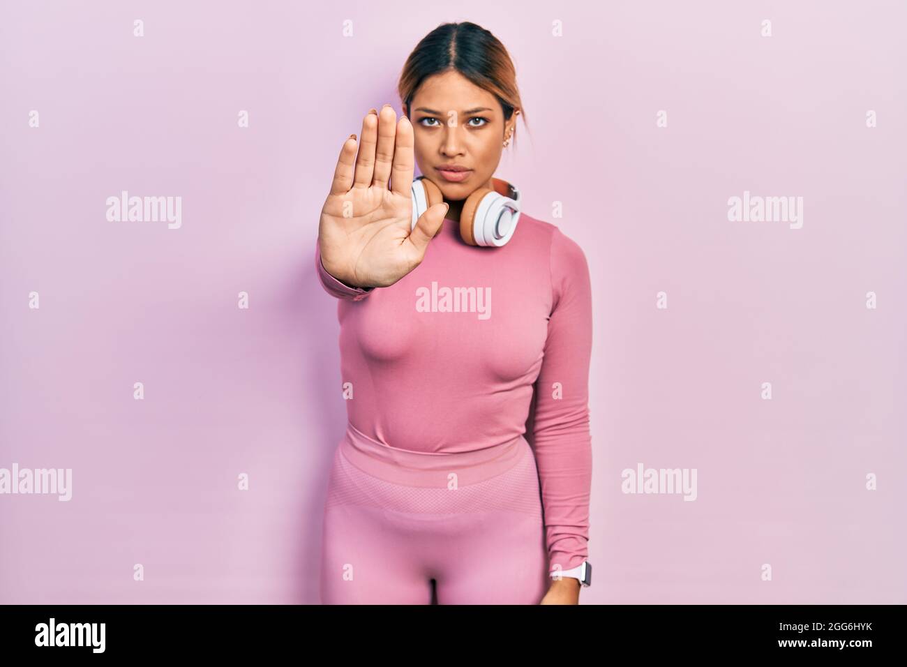 Beautiful hispanic woman wearing gym clothes and using headphones doing ...