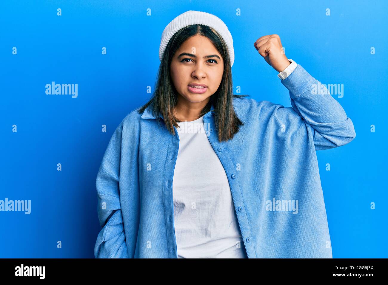 Young latin woman wearing cute wool cap angry and mad raising fist ...