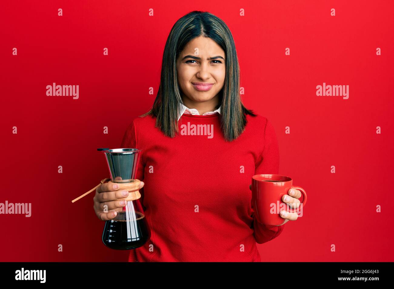 Young latin woman holding coffee filter and cup clueless and confused ...
