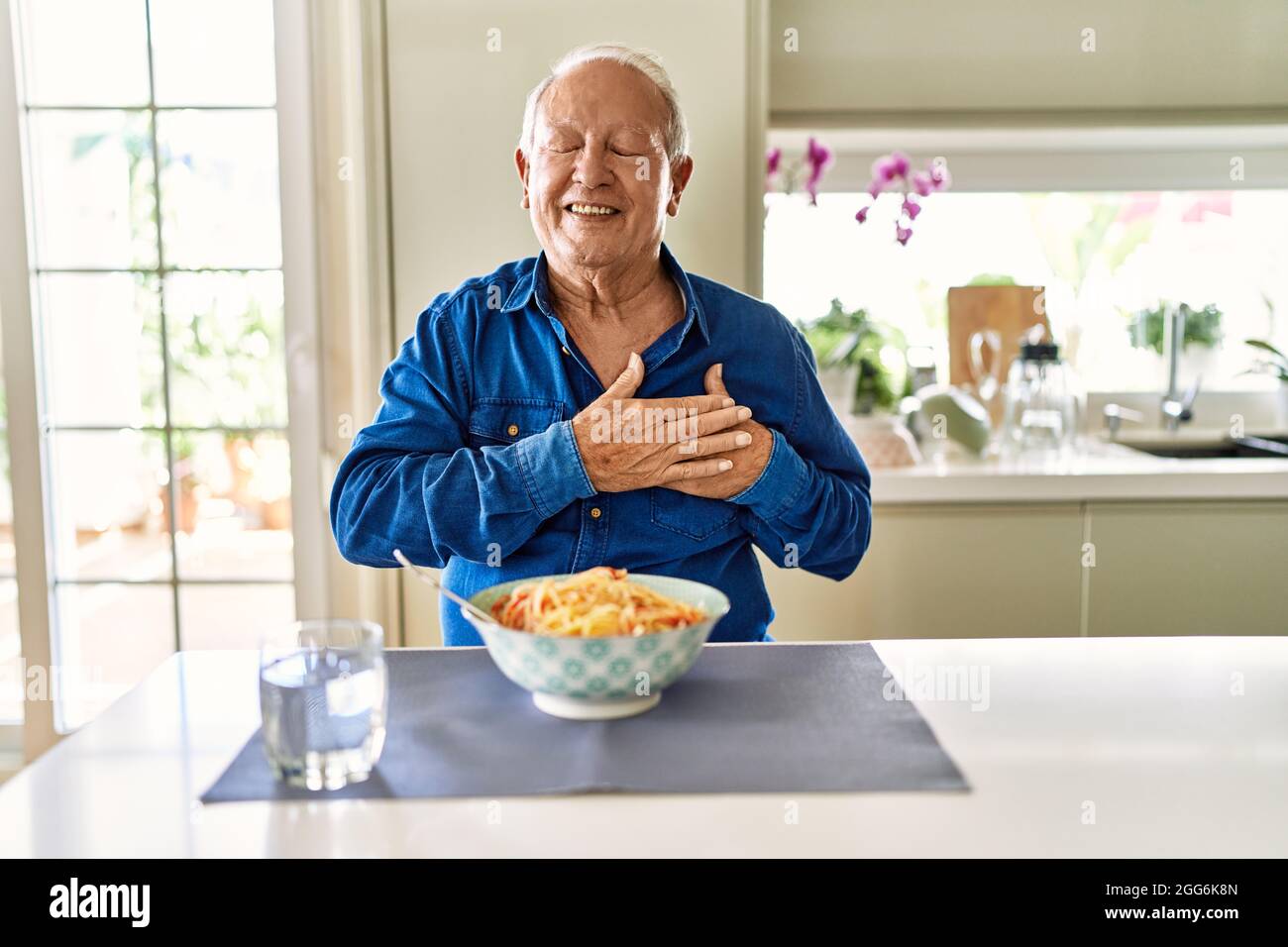 Senior man with grey hair eating pasta spaghetti at home smiling with ...