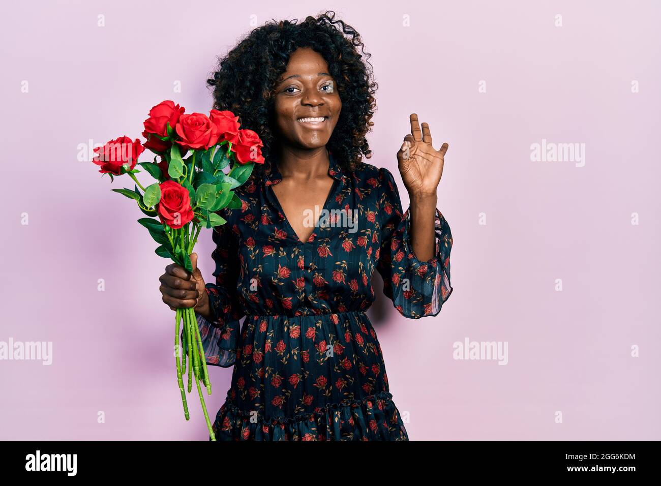 Young african american woman holding bouquet of red roses doing ok sign ...