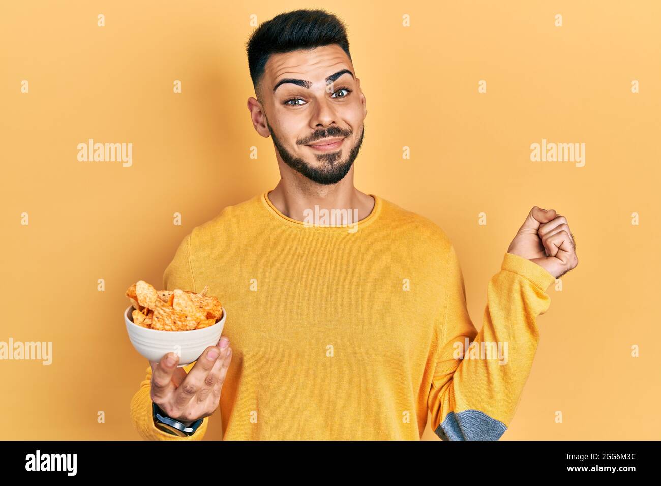 Young hispanic man with beard holding nachos potato chips screaming ...