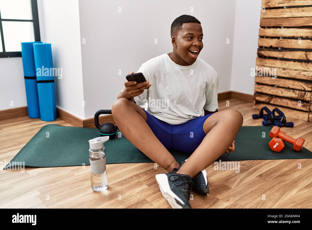 Young african man sitting on training mat at the gym using smartphone ...