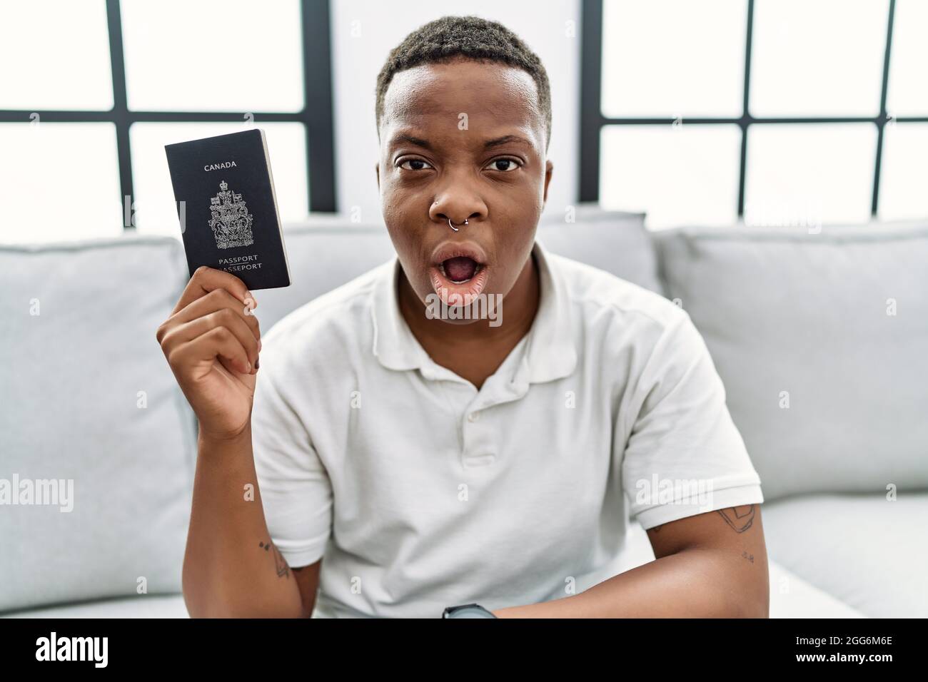 Young African Man Holding Canada Passport Scared And Amazed With Open Mouth For Surprise