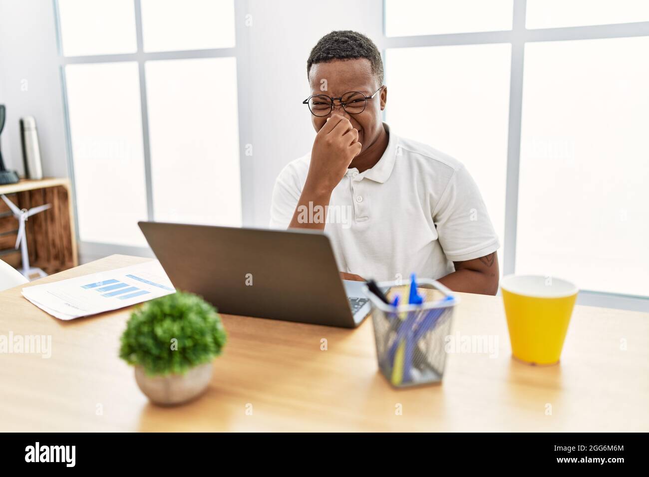 Young african man working at the office using computer laptop smelling ...