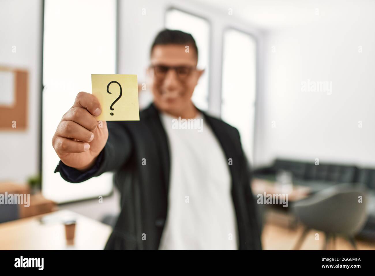 Young latin businessman smiling happy holding question mark reminder at ...