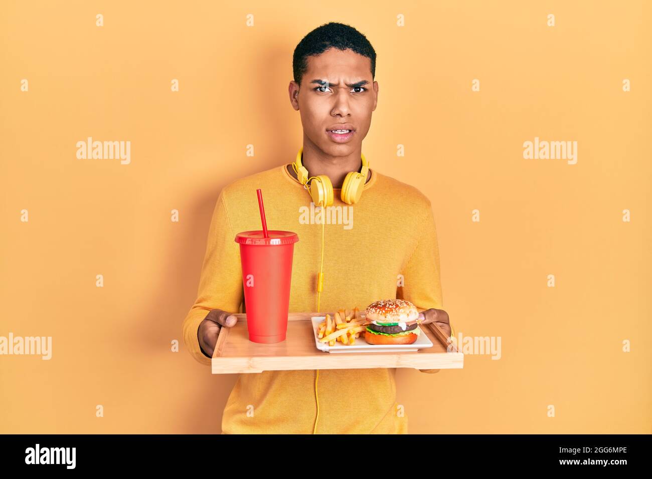 Young african american guy eating a tasty classic burger in shock face ...