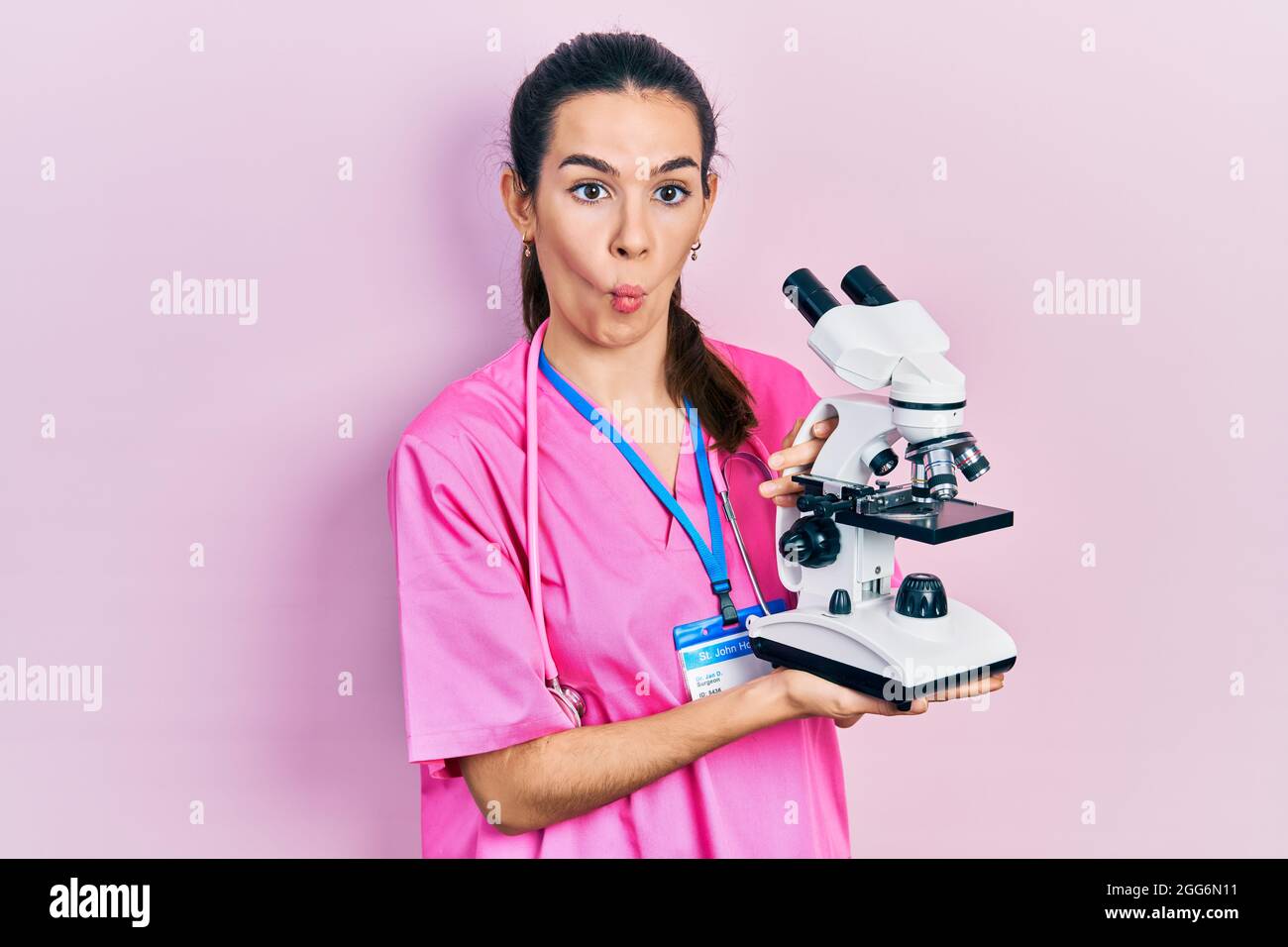 Young brunette woman holding microscope making fish face with mouth and ...