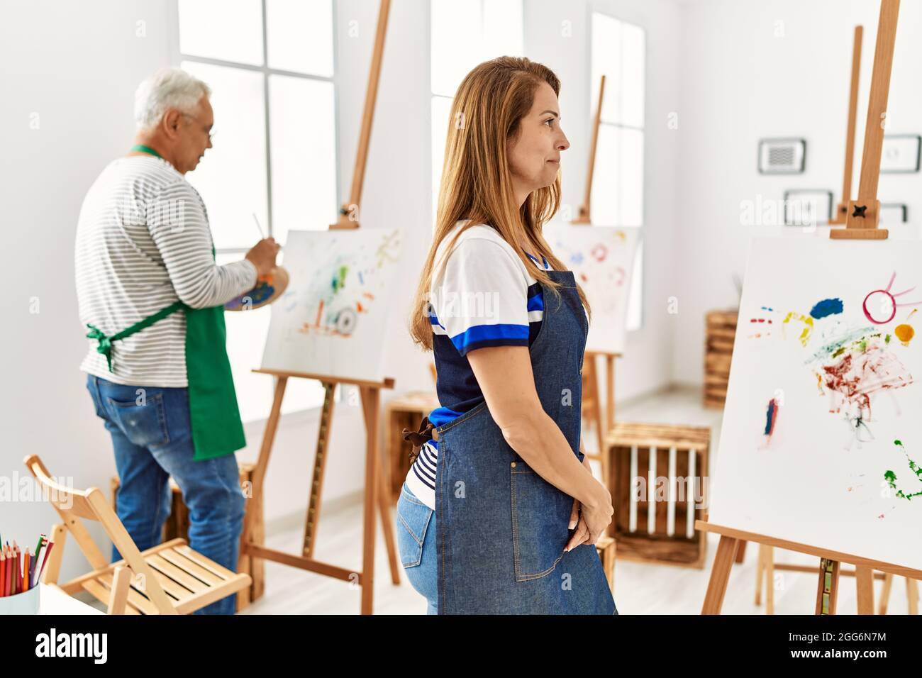 Hispanic woman wearing apron at art studio looking to side, relax profile pose with natural face ...