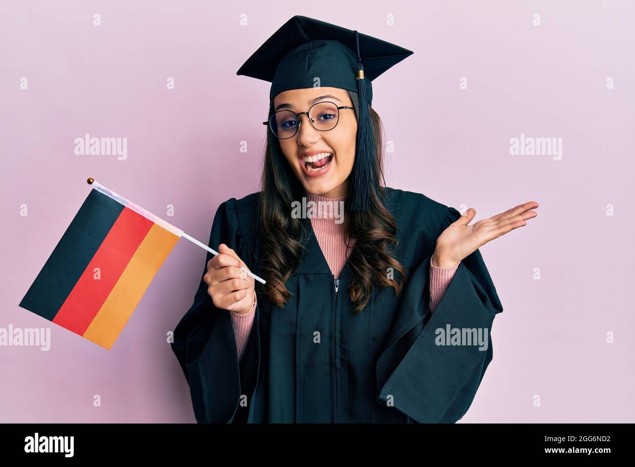Young hispanic woman wearing graduation uniform holding germany flag ...