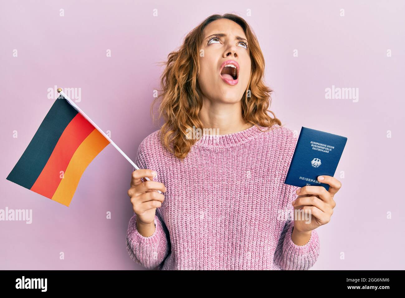 Young caucasian woman holding germany flag and passport angry and mad ...