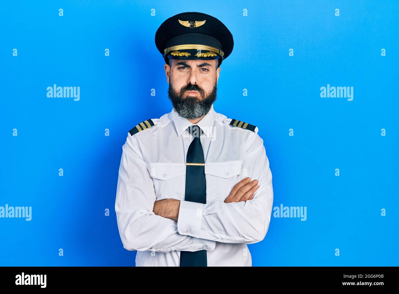 Young hispanic man wearing airplane pilot uniform with arms crossed ...