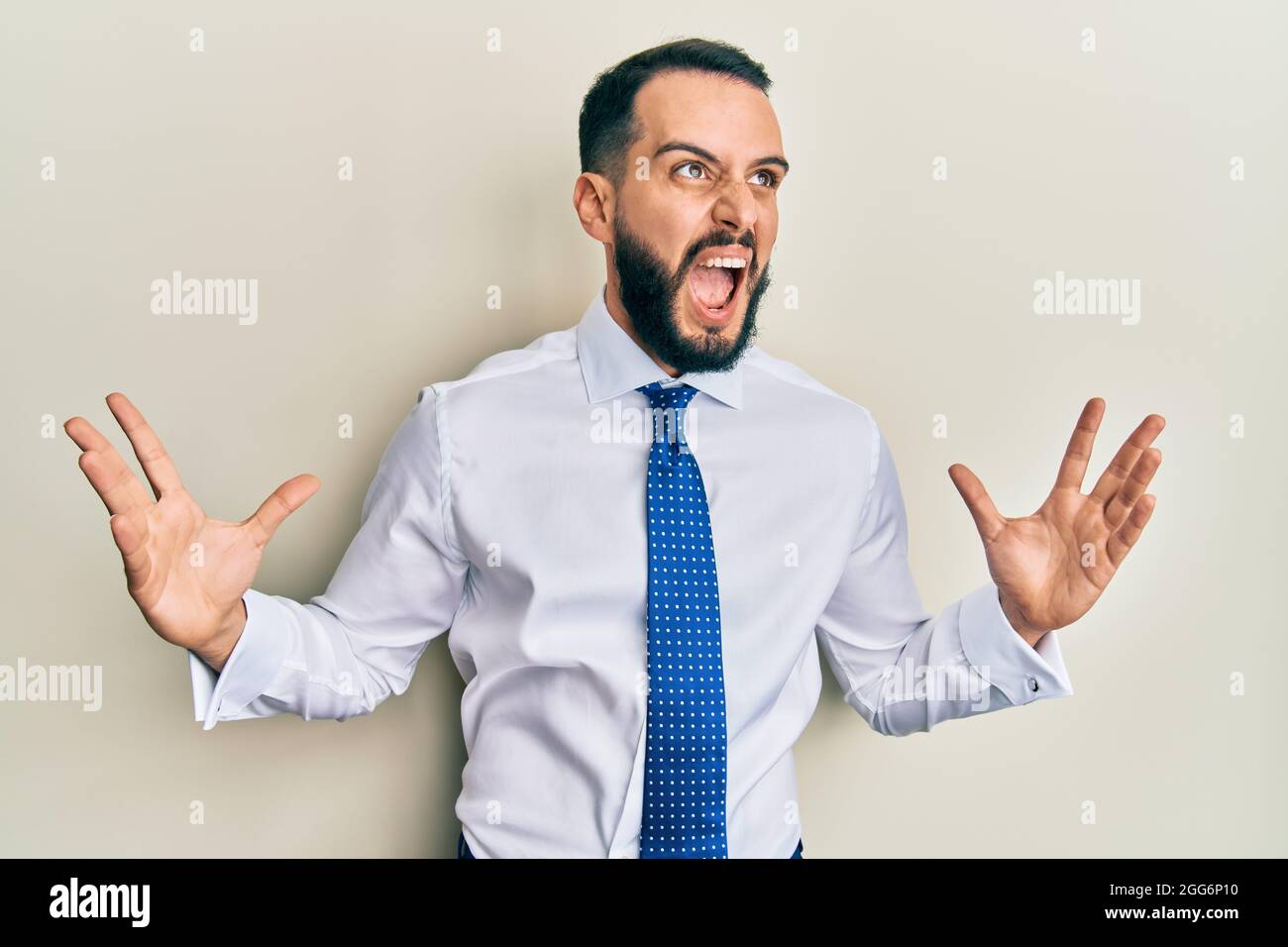 Young man with beard wearing business tie crazy and mad shouting and ...