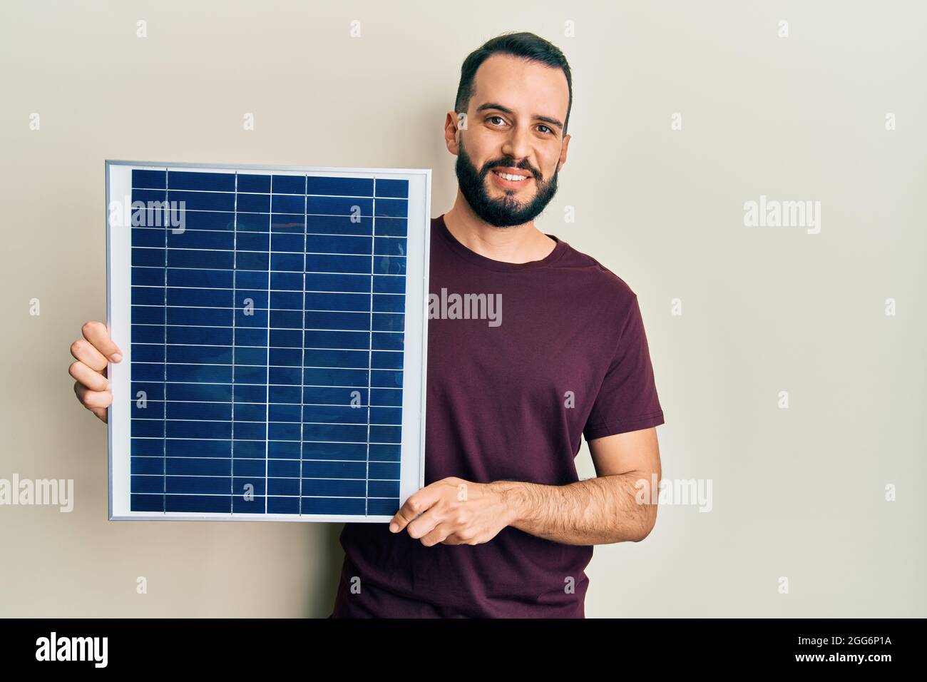 Young man with beard holding photovoltaic solar panel looking positive ...