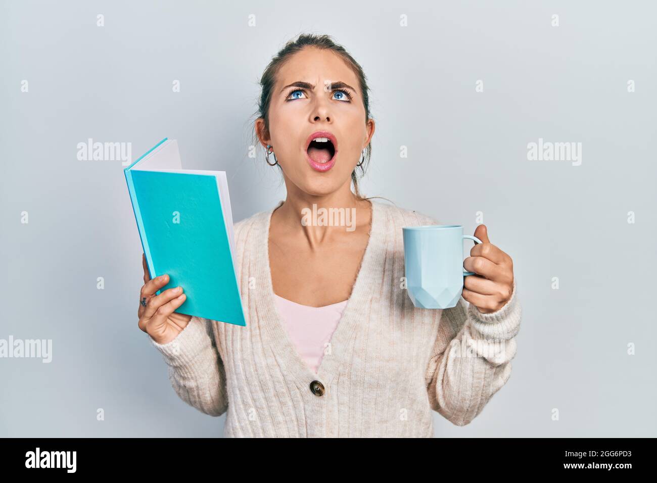 Beautiful caucasian woman with blond hair reading a book and drinking a ...