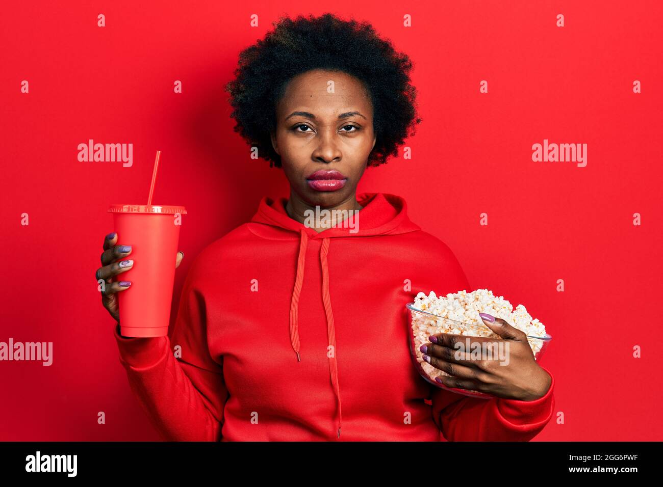 Young african american woman eating popcorn and drinking soda skeptic ...