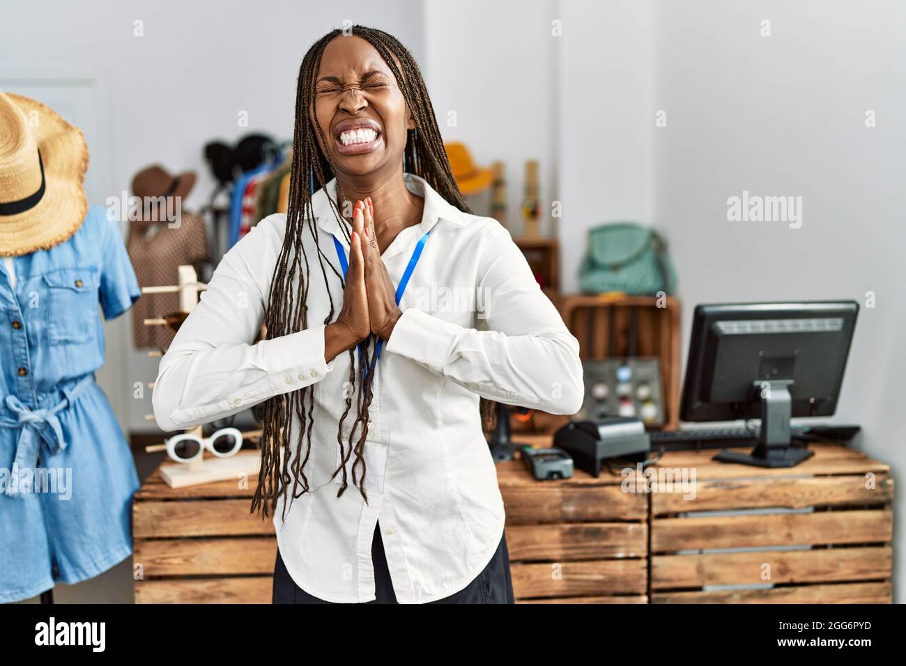 Black woman with braids working as manager at retail boutique begging and praying with hands ...