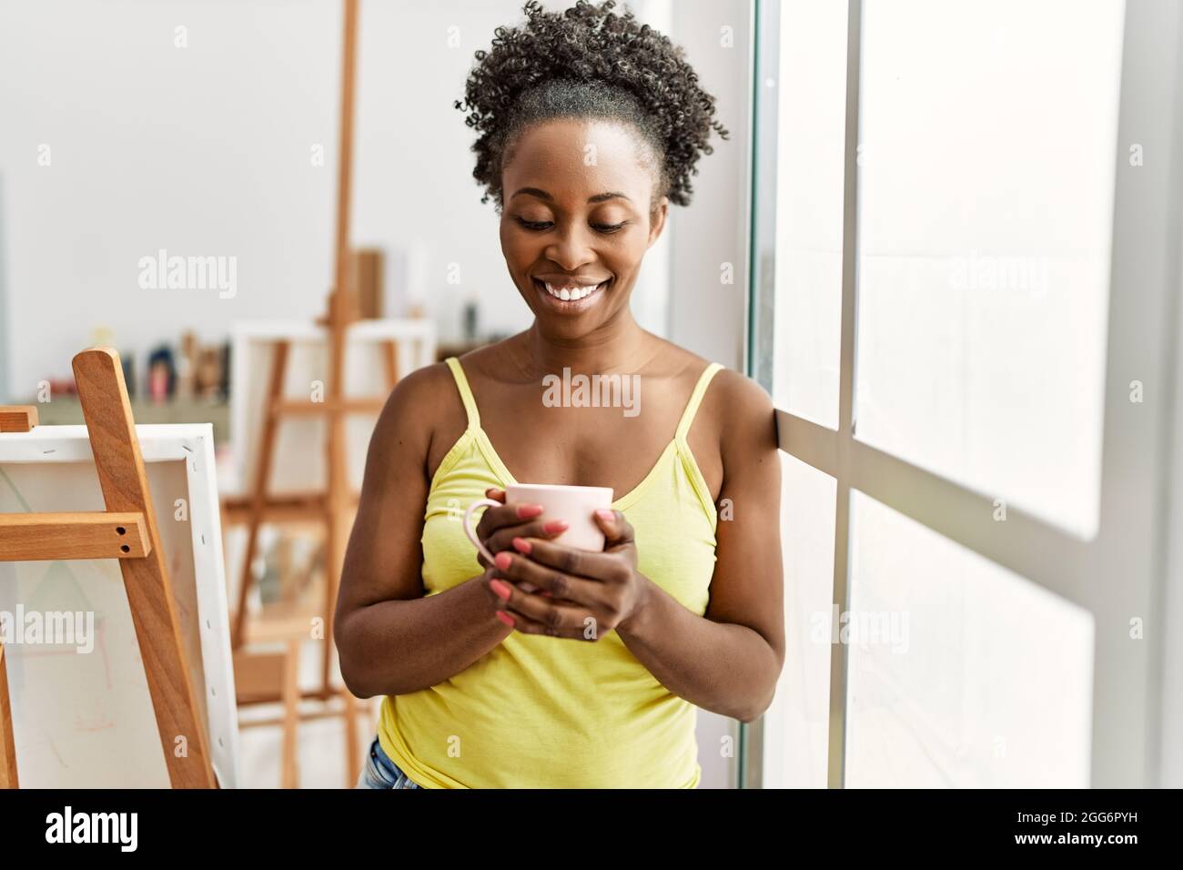 Young african american artist woman drinking coffee standing at art ...
