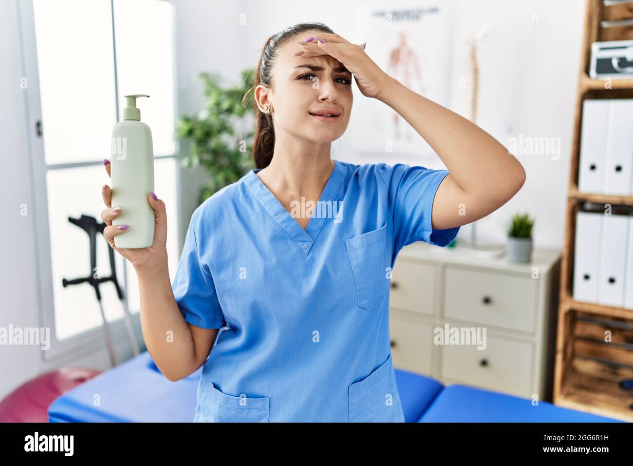 Young physiotherapist woman holding massage body lotion stressed and ...
