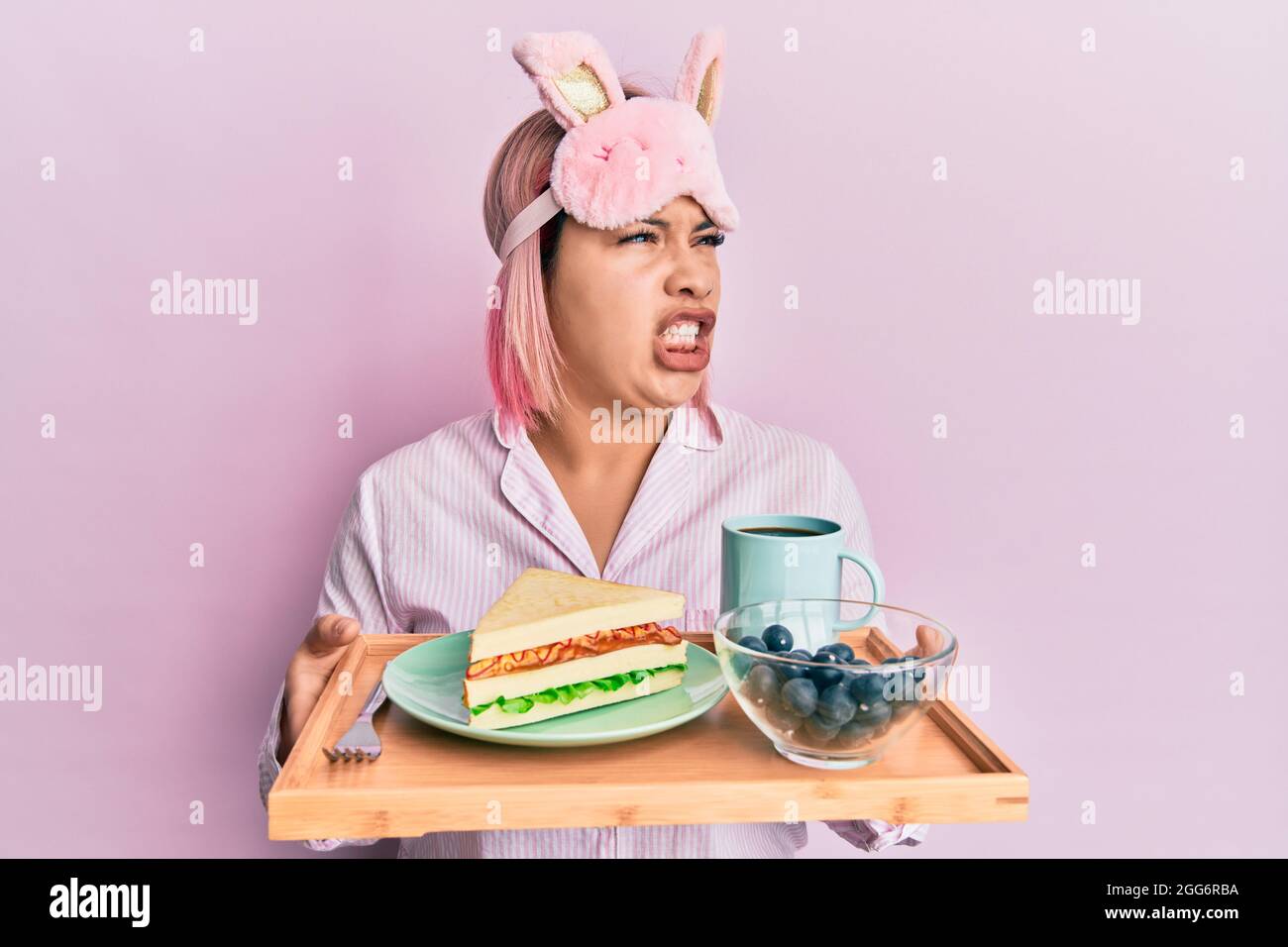 Hispanic woman with pink hair wearing pajama holding healthy breakfast ...