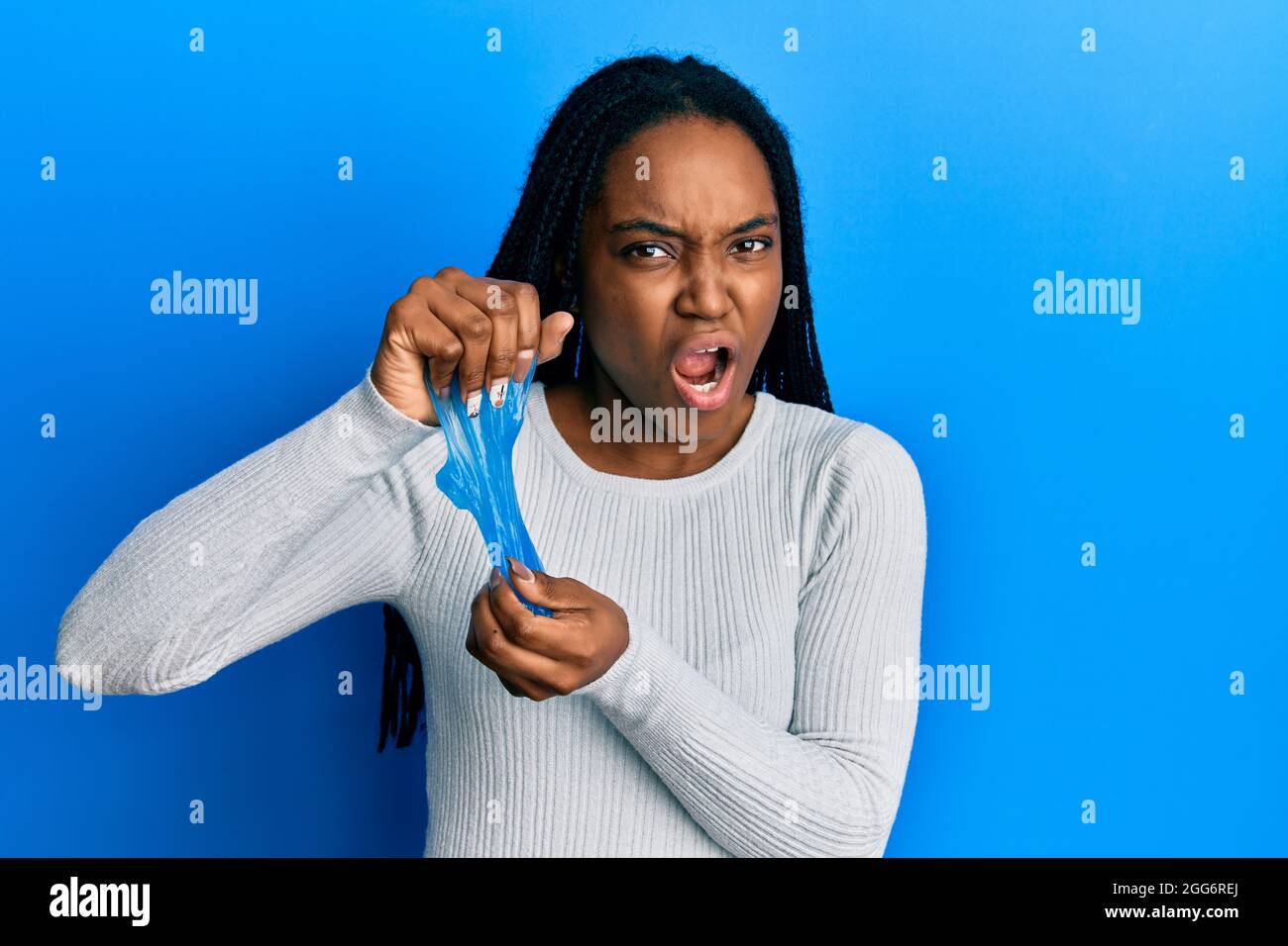 African american woman with braided hair holding slime in shock face ...