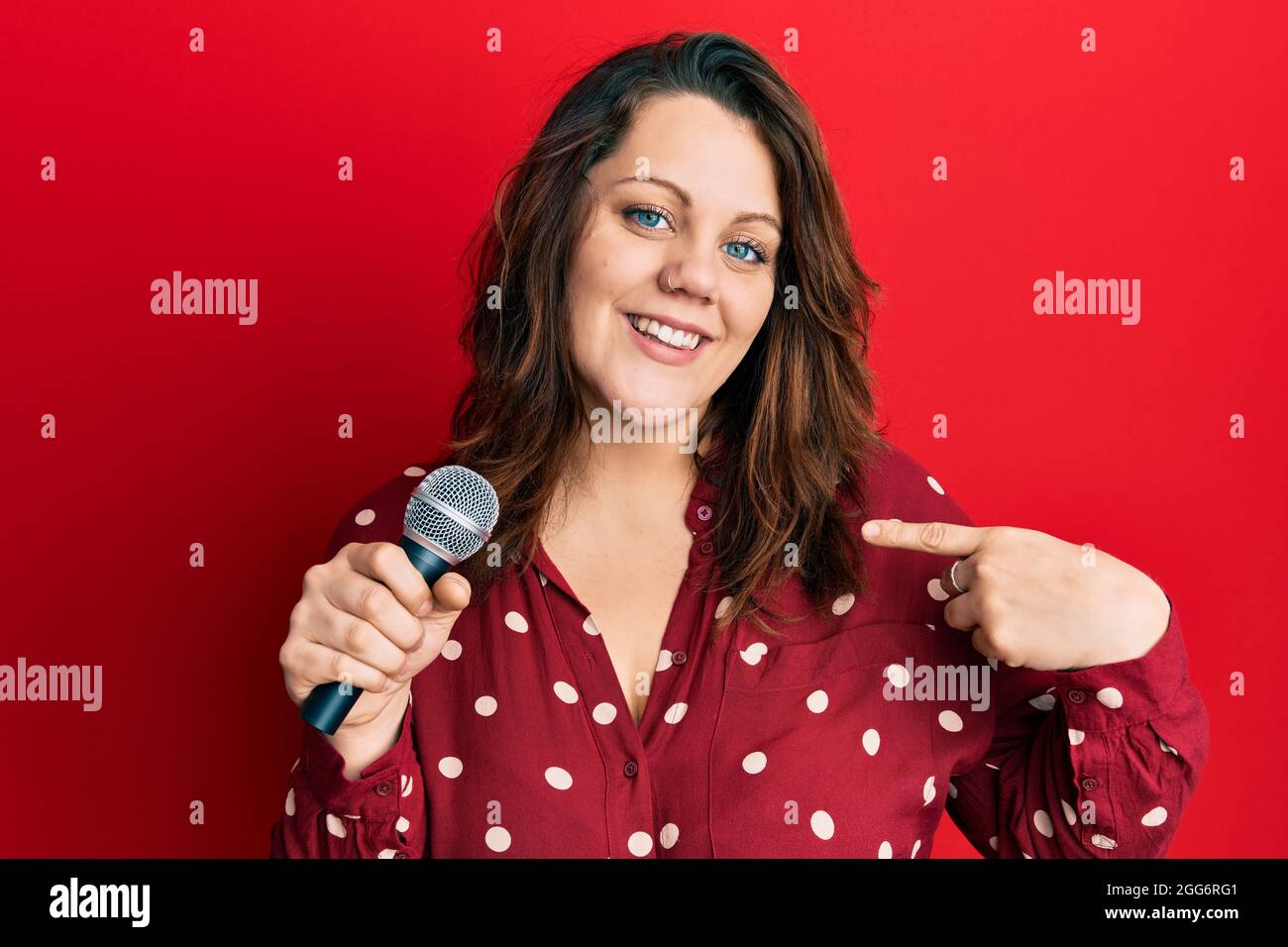 Young caucasian woman singing song using microphone pointing finger to ...