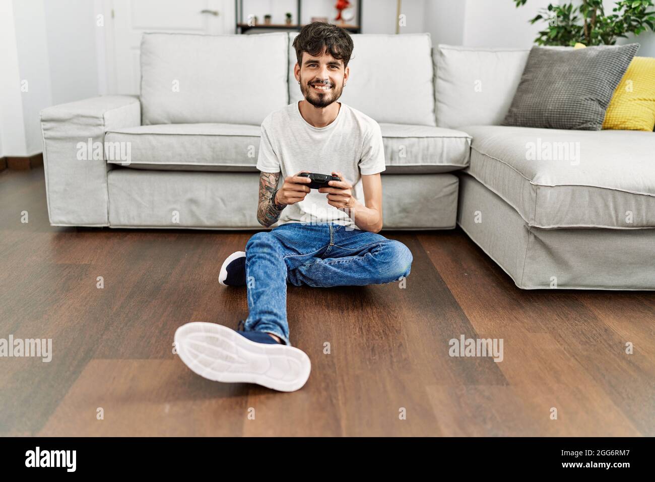 Young hispanic man playing video game sitting on the floor at home ...