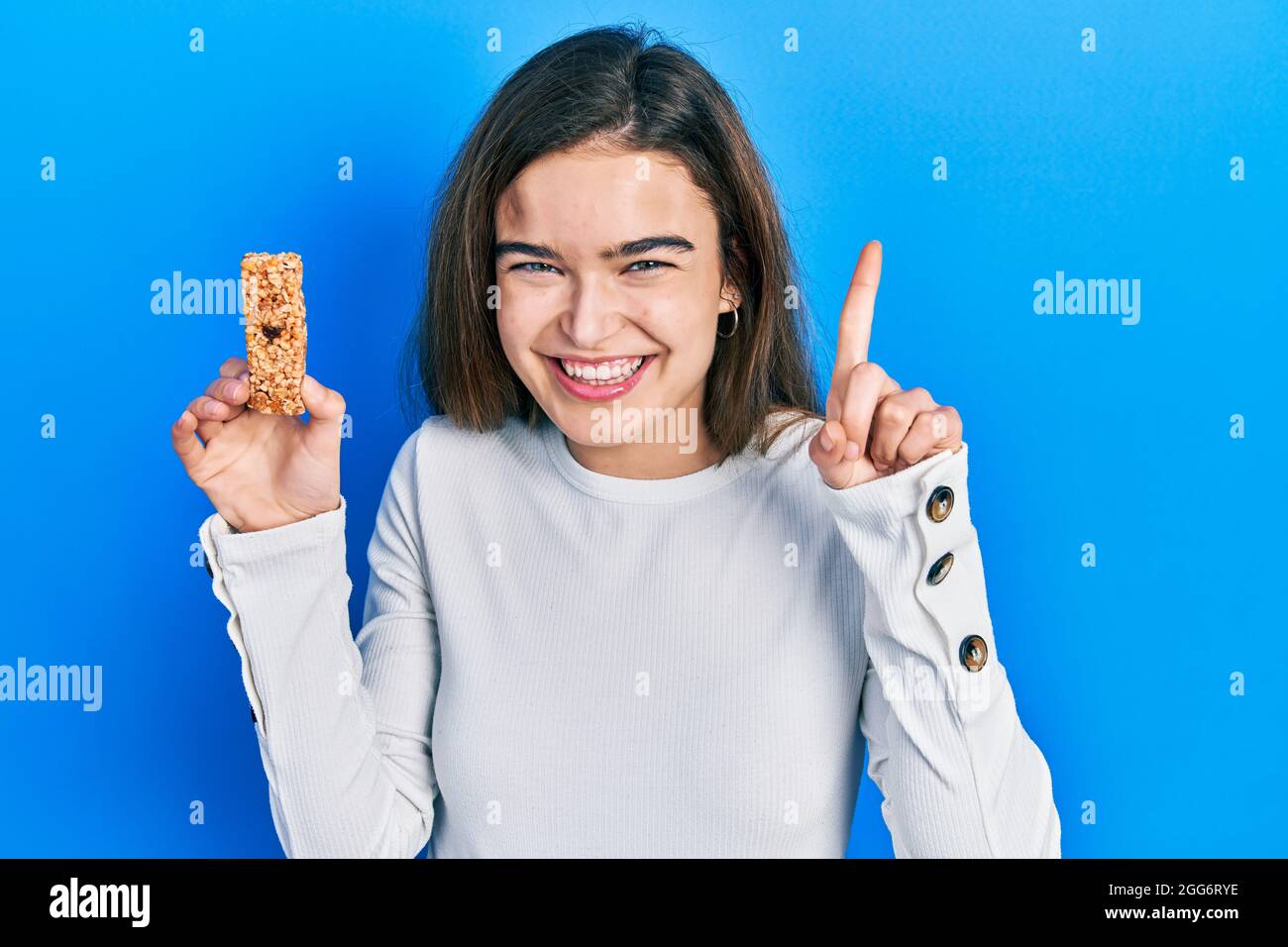 Young caucasian girl eating protein bar as healthy energy snack smiling ...