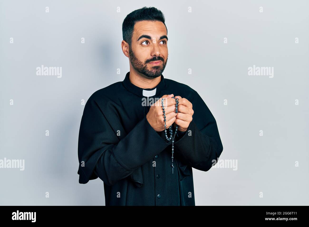Handsome hispanic priest man with beard praying holding catholic rosary ...