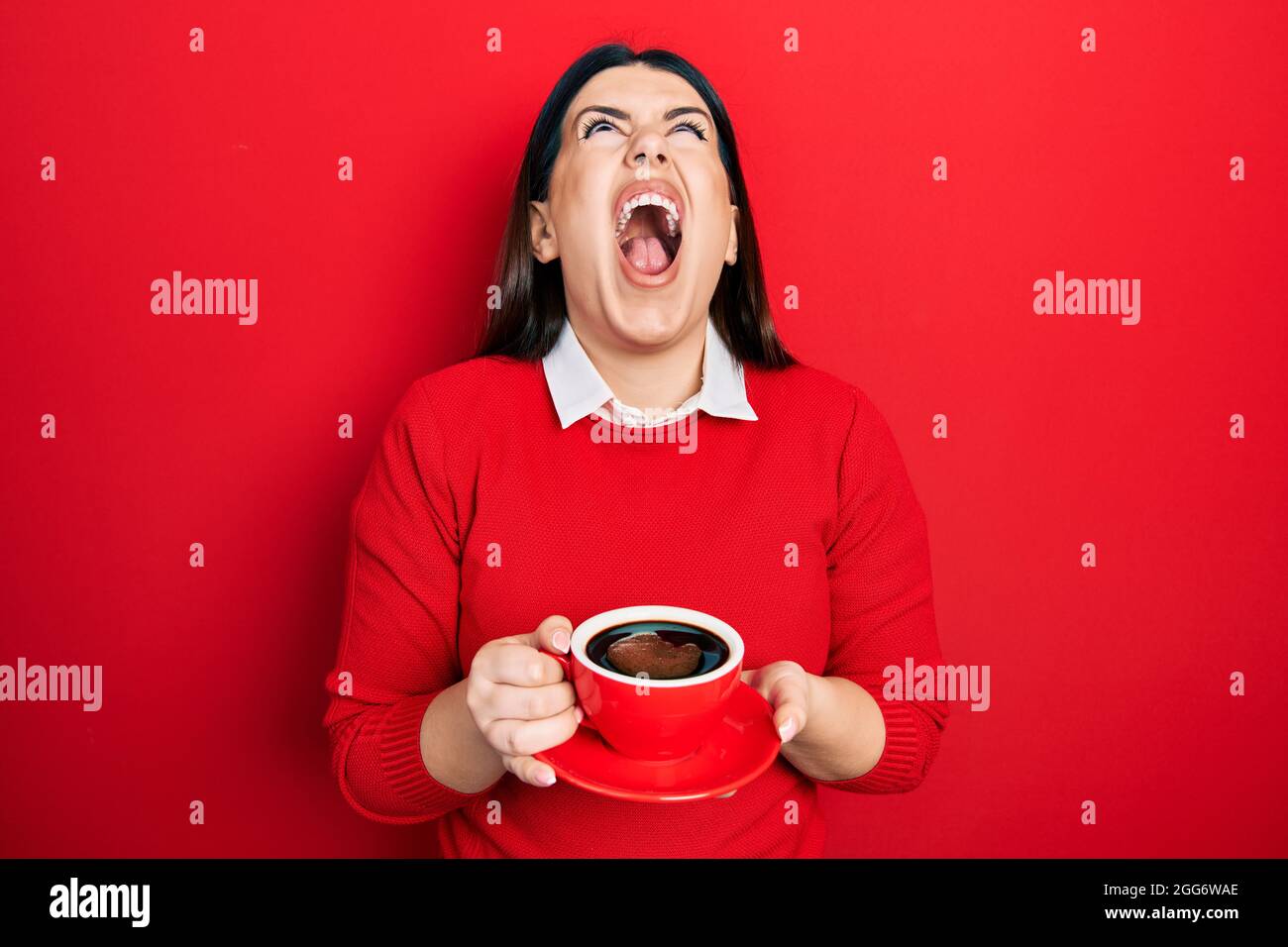 Young hispanic woman drinking a cup of coffee angry and mad screaming ...