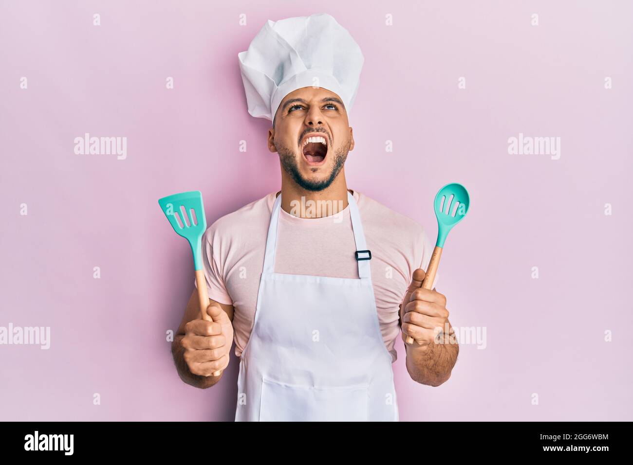 Young arab man wearing professional cook apron and hat holding spoon ...